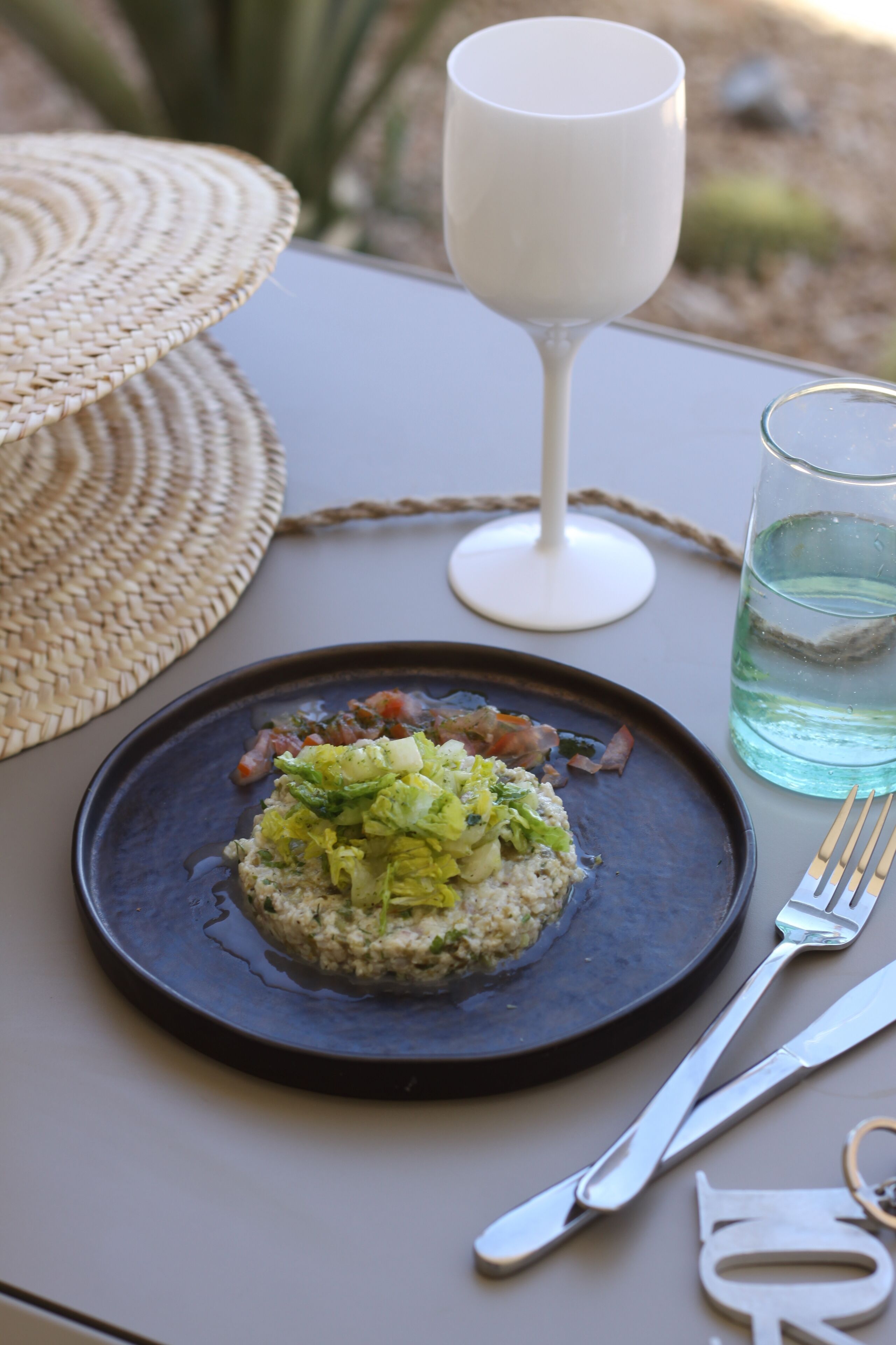 Uma mesa com um prato de comida, um copo de água e talheres.