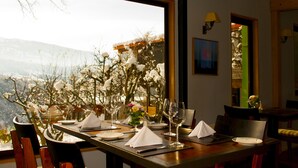 Mesa de jantar posta para refeição, com vista para montanhas através de uma grande janela.