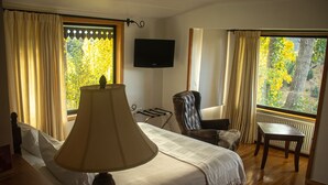 Quarto de hotel com cama, uma cadeira, uma mesa, televisão e cortinas.
