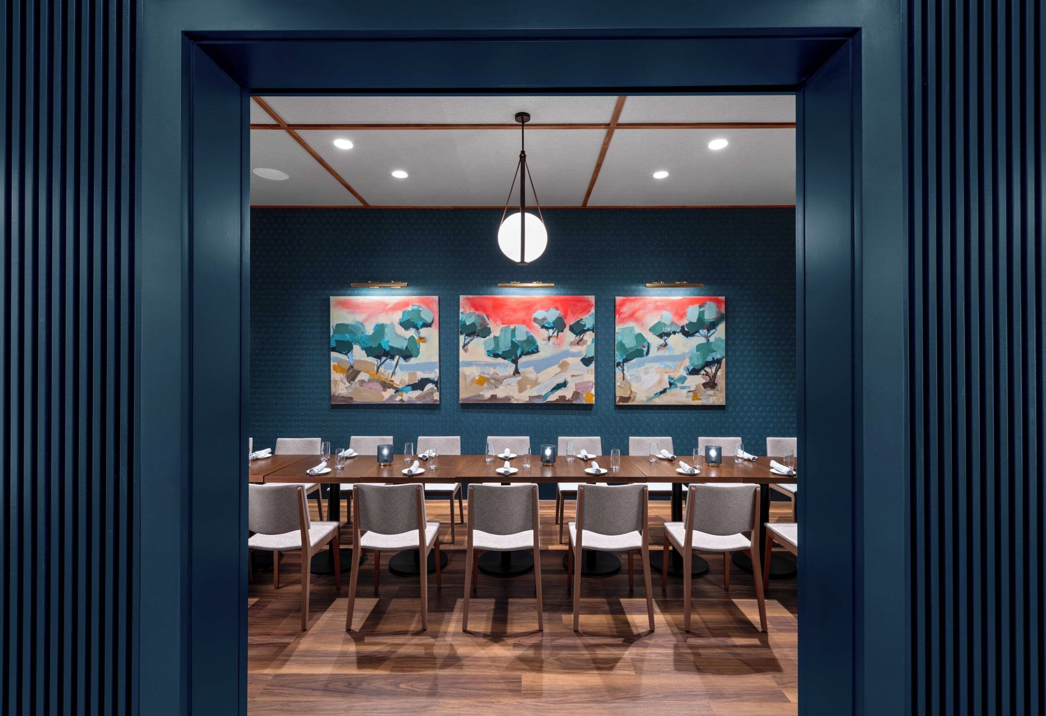 Uma sala de conferências com uma mesa comprida, cadeiras e três pinturas abstratas na parede.