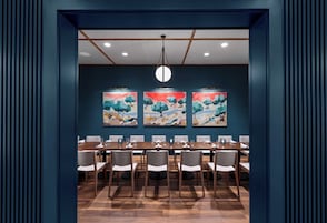 Uma sala de conferências com uma mesa comprida, cadeiras e três pinturas abstratas na parede.