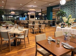 Um restaurante com várias mesas e cadeiras, piso de madeira e iluminação pendente.