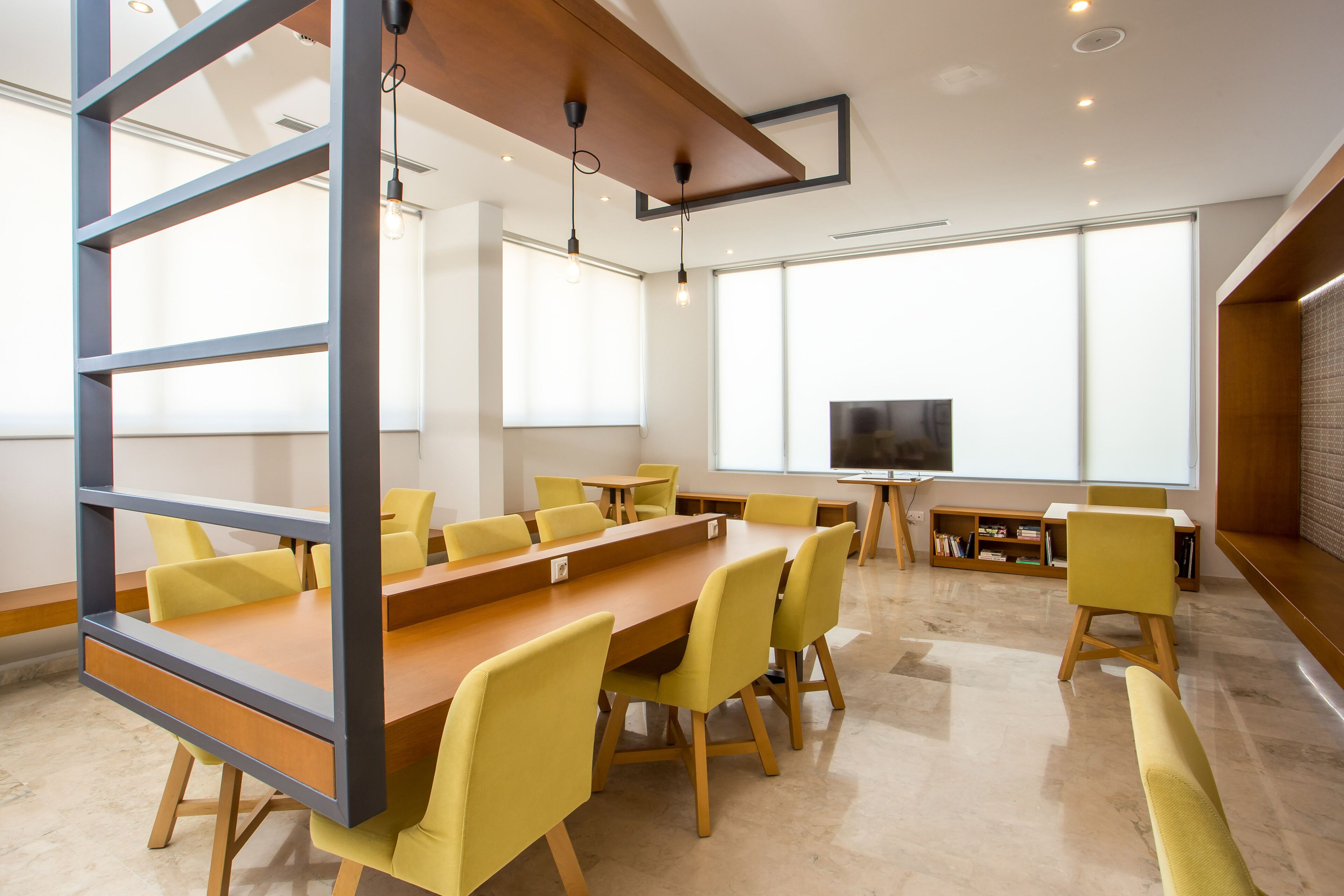 Sala de conferências moderna com uma mesa comprida, cadeiras amarelas, uma televisão e uma estante de livros.