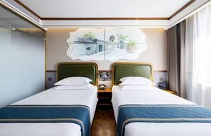 Quarto de hotel com duas camas, uma obra de arte na parede, um telefone e uma mesa de cabeceira.