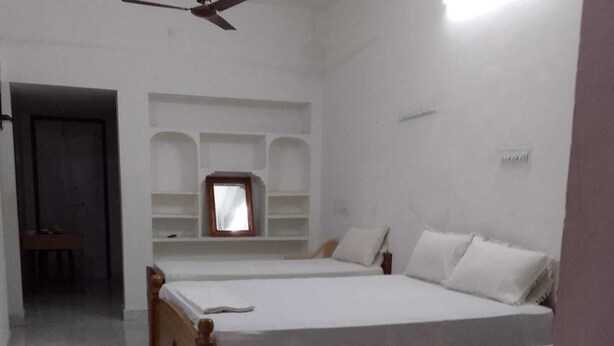 Quarto com duas camas de madeira, um ventilador de teto, uma janela pequena e um armário embutido.