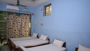 Quarto com quatro camas de solteiro, ventilador de teto, aparelhos de ar condicionado e janela com grades.