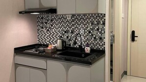 Uma cozinha compacta com armários cinza, bancada preta e painel de azulejos.