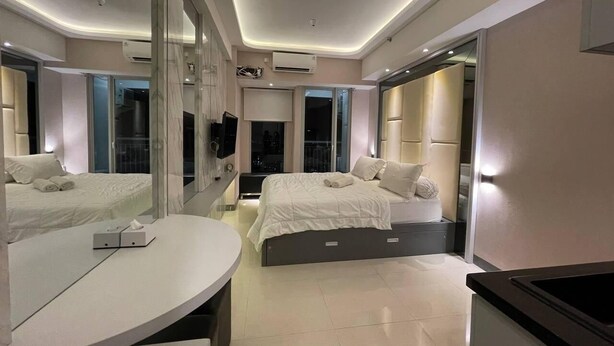 Quarto de hotel moderno com duas camas, um espelho grande e uma toucador redonda no banheiro.