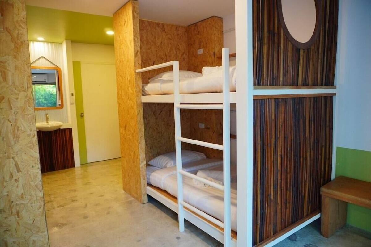Quarto com beliche, painel de parede de madeira, um banco e pia no canto.