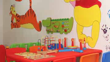 Um espaço de brincadeiras infantil com mobiliário colorido, um grande mural e brinquedos educativos.