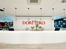 Uma receção com o letreiro 'DORMERO', um interior moderno e uma parede com fotografias emolduradas.