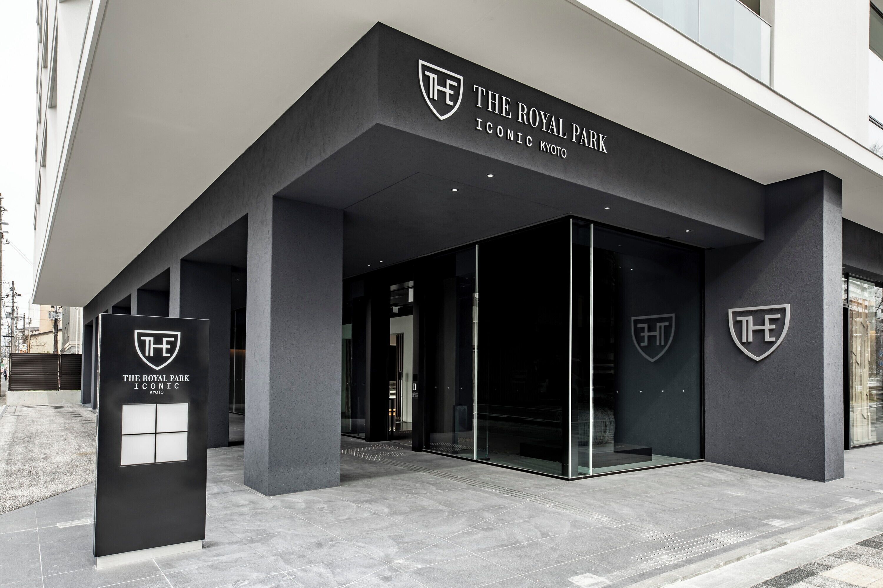 Entrada moderna de hotel com fachada escura e portas de vidro.