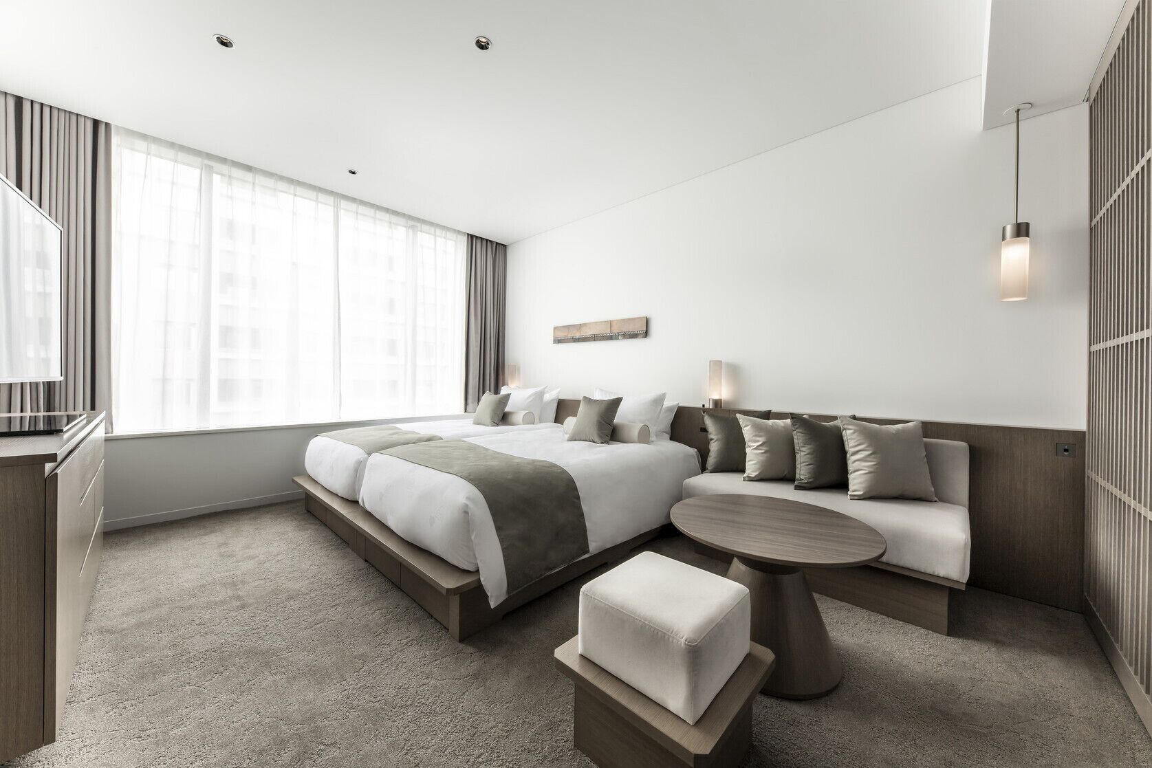 Quarto de hotel moderno com uma cama grande, um sofá, uma mesinha e uma televisão.