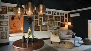 Quarto com uma mesa redonda de madeira, um sofá e um abajur. As paredes são decoradas com quadros emoldurados.