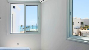 Quarto com uma janela ampla que oferece vista para o mar e varanda com plantas em vasos.