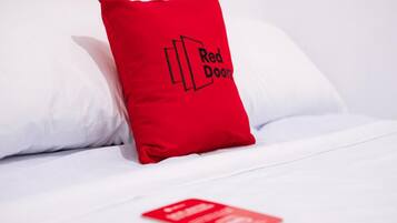 Cama com roupa de cama branca e travesseiro vermelho com a inscrição 'Red Door'.
