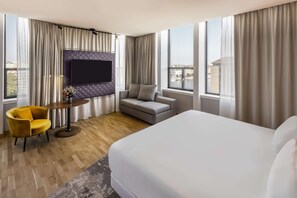 Quarto de hotel com uma cama grande, um sofá, uma mesinha e uma televisão.