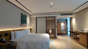 Quarto de hotel moderno com uma cama grande, mesa de cabeceira, abajur e uma pequena escrivaninha com cadeira.