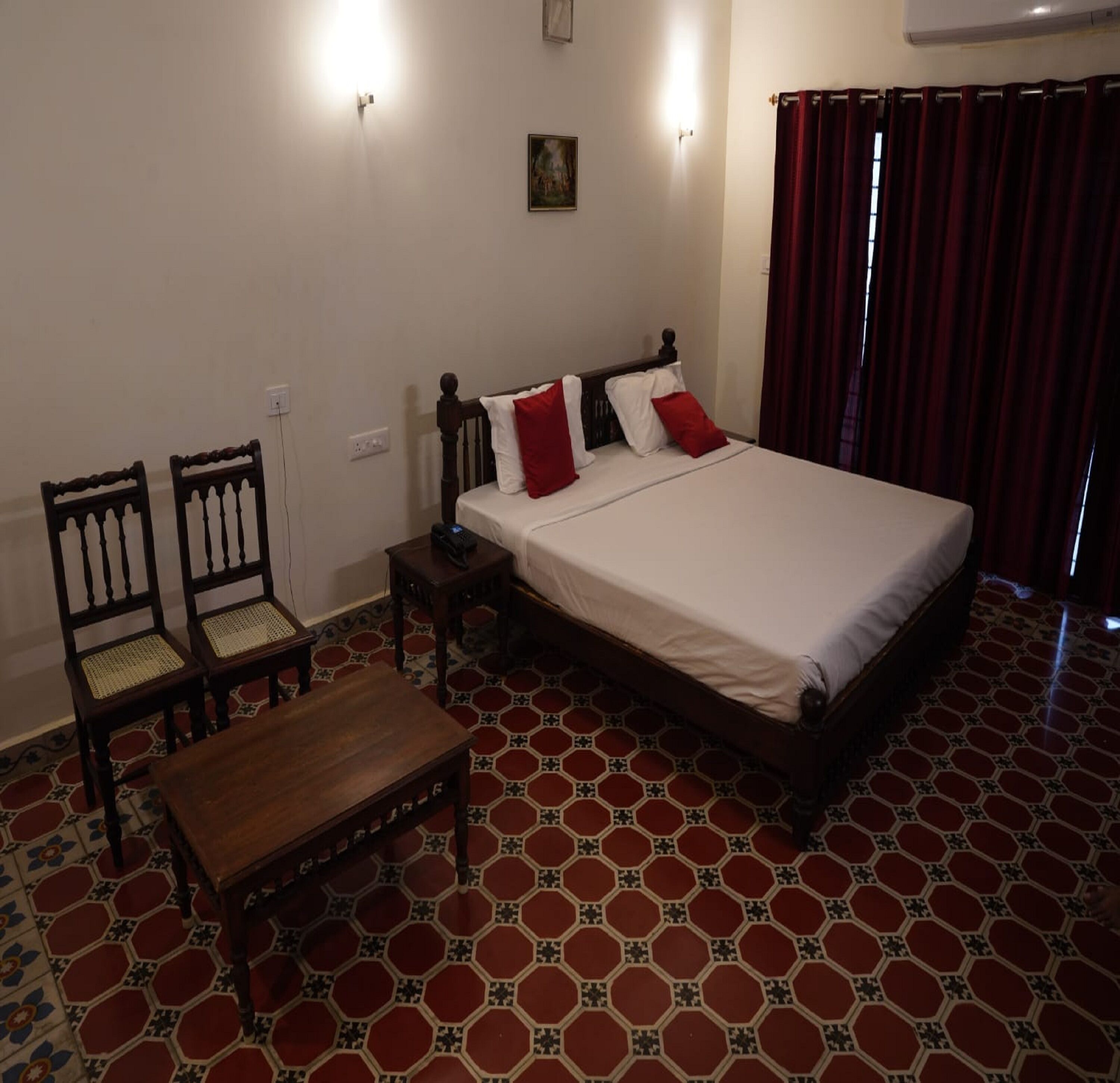 Quarto com cama, duas cadeiras de madeira, uma mesinha e piso estampado.
