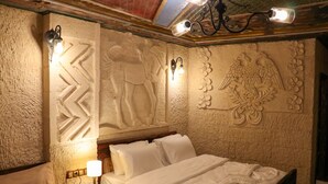 Quarto com cama, mesa de cabeceira e esculturas nas paredes.