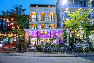 Um edifício com várias varandas, uma fileira de bicicletas estacionadas na frente e uma placa indicando um restaurante ou café.
