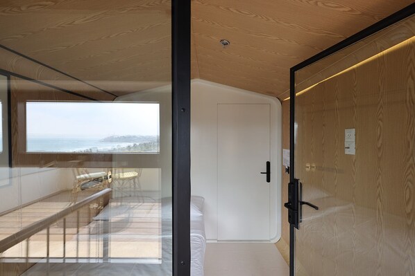 Quarto moderno com uma janela grande que oferece vista para o mar, uma cama e um painel de vidro.