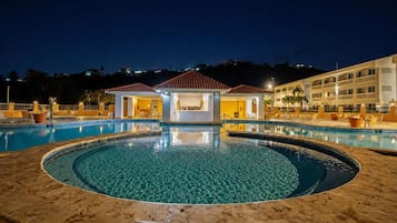 Uma piscina com design circular, área de estar coberta e um edifício ao fundo.