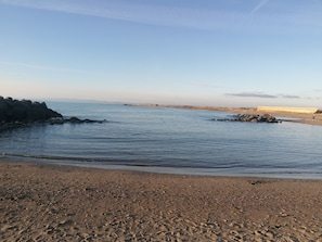 Uma praia com água cristalina, afloramentos rochosos e uma faixa de areia.