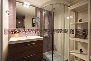 Uma casa de banho moderna com cabine de duche em vidro, toucador com espelho e painel de azulejos.