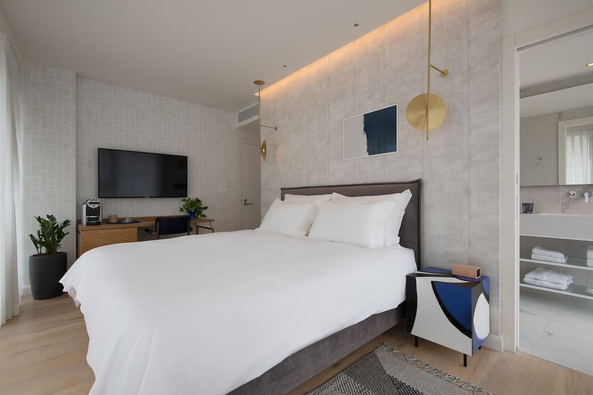 Quarto moderno com uma cama grande, uma televisão de tela plana, uma mesa de cabeceira com abajur e um armário embutido.