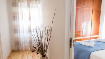 Quarto com piso de madeira, uma cama com colcha azul, guarda-roupa de madeira e um vaso com planta.