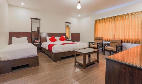 Quarto de hotel com duas camas de solteiro, um sofá, uma mesinha e uma janela grande com cortinas.