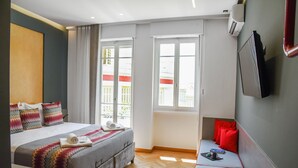 Quarto de hotel com cama, área de estar e televisão na parede.