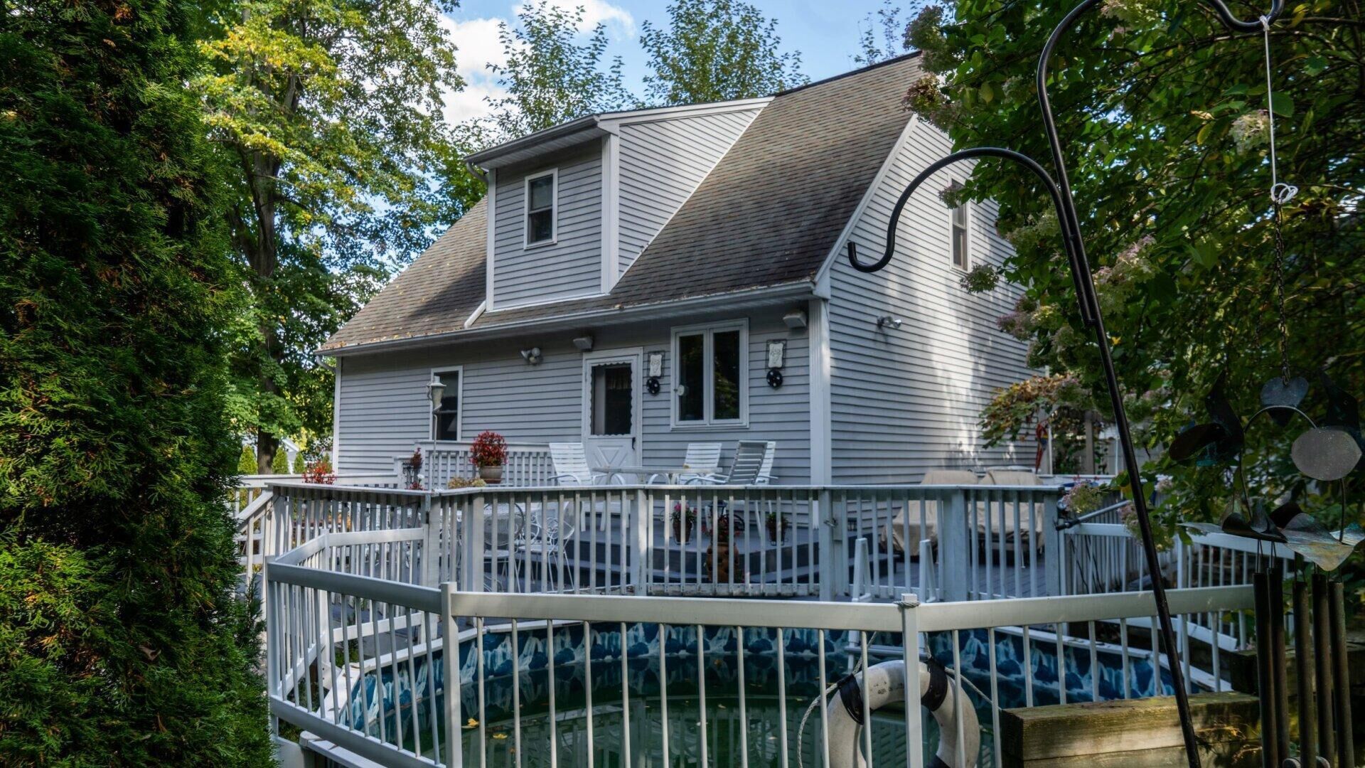 Uma casa de dois andares com deck cercado e piscina.