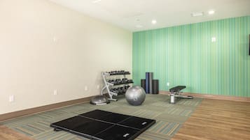 Sala de ginástica com colchonete, halteres, bola de exercício e um banco.