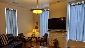 Uma sala de estar com sofá, poltronas, mesa de centro, lareira, televisão e lustre.