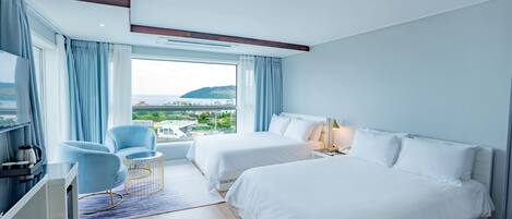Quarto de hotel moderno com duas camas, televisão, escrivaninha e vista para a cidade.
