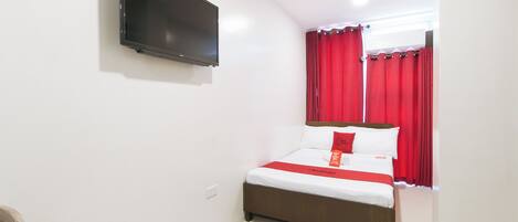 Quarto de hotel com uma cama, televisão fixada na parede e cortinas vermelhas.