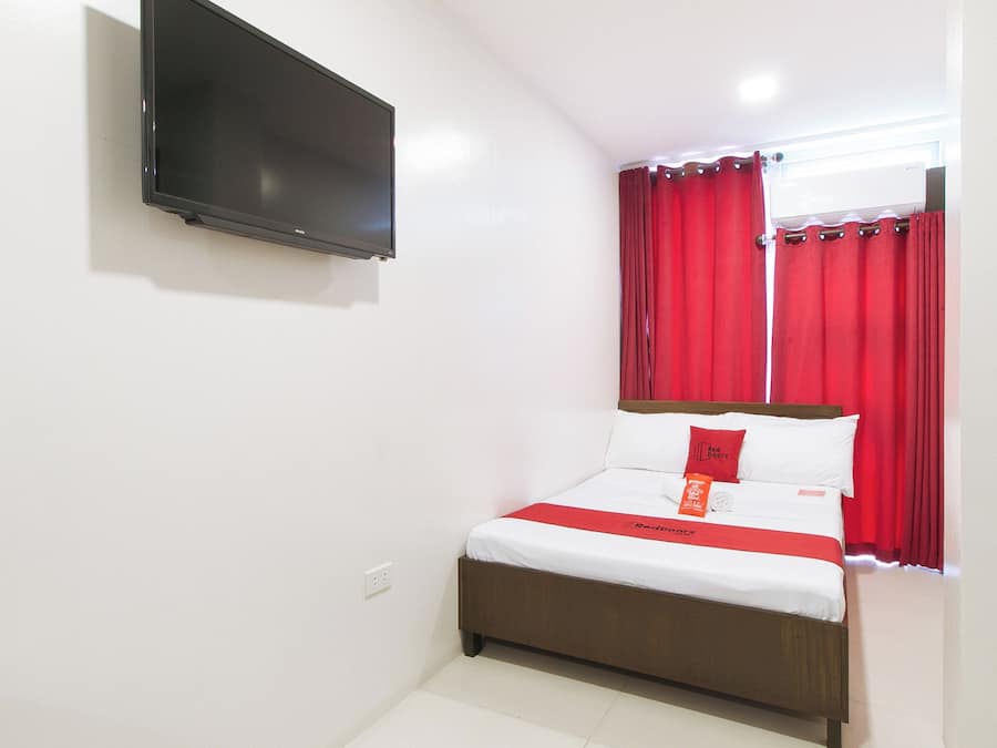 Quarto de hotel com uma cama, televisão fixada na parede e cortinas vermelhas.