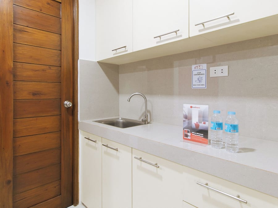 Cozinha com porta de madeira, pia de aço inoxidável e bancada com sinal de desconto RedDoorz e garrafas de água.