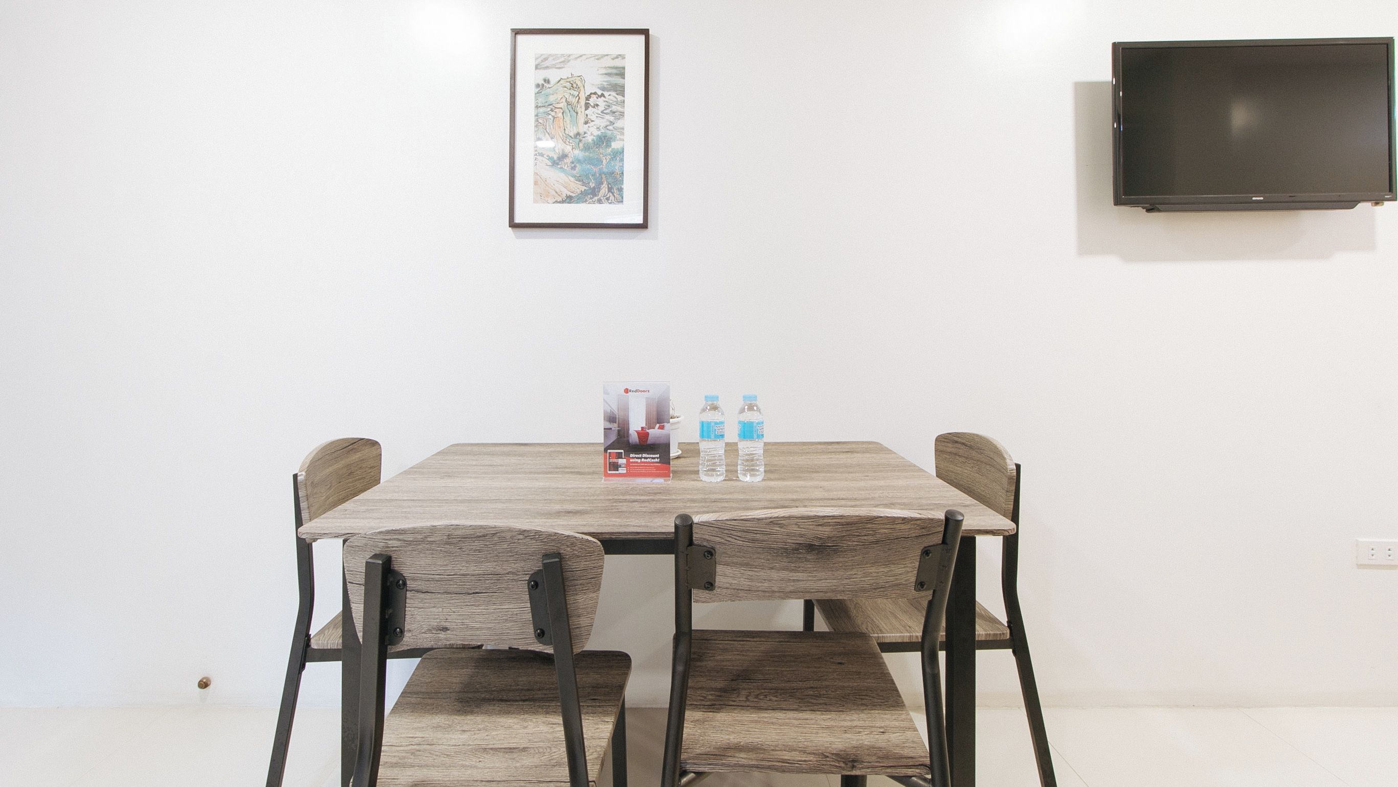 Uma área de jantar com uma mesa de madeira, quatro cadeiras, duas garrafas de água e um quadro pendurado na parede.