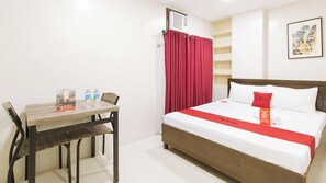 Quarto de hotel com cama de madeira, cortina vermelha, mesa com garrafas de água e quadro na parede.