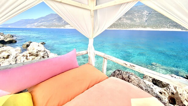 Uma cama com almofadas coloridas e vista para o mar e as montanhas.