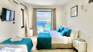 Quarto de hotel com cama, televisão, ar condicionado, janela com cortinas e vista para o exterior.
