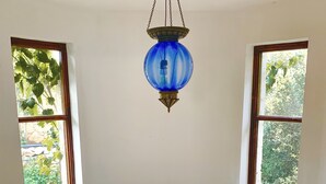 Quarto com luminária pendente azul, porta de madeira e vista para degraus de pedra que levam para o exterior.