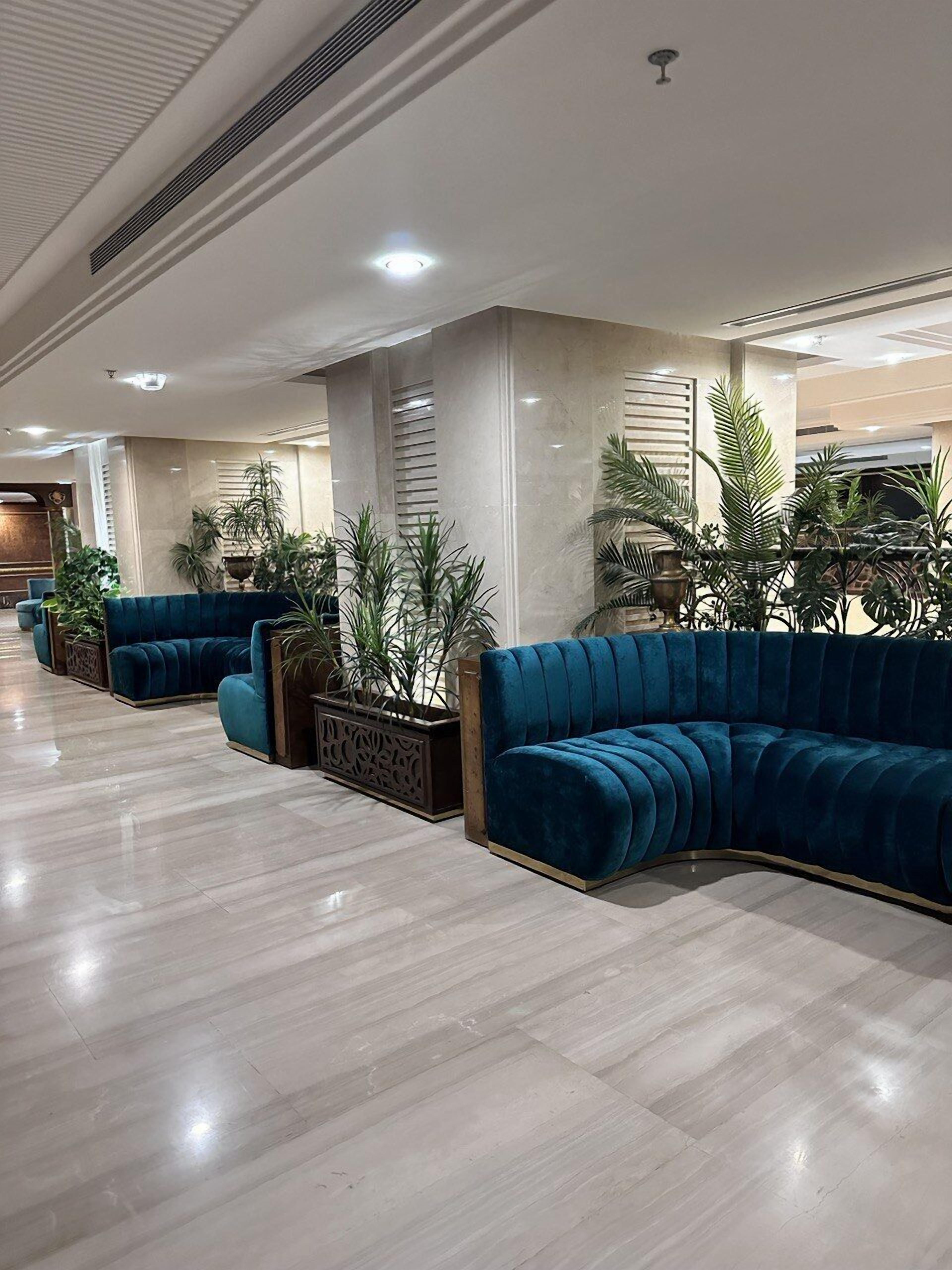 Um hall amplo com um sofá azul curvo, plantas em vasos e piso de mármore polido.