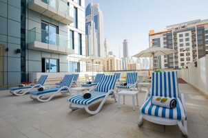 Um lounge no terraço com espreguiçadeiras e guarda-sóis, com vista para um horizonte urbano repleto de edifícios modernos.