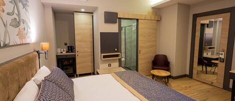 Quarto de hotel com cama, escrivaninha, cadeira, mesinha, espelho e guarda-roupa.