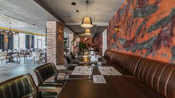Restaurante com uma longa mesa de madeira, assentos em cabines de couro e luminárias pendentes.