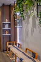 Quarto com piso de madeira, um banco, uma estante com objetos decorativos e uma planta pendente.
